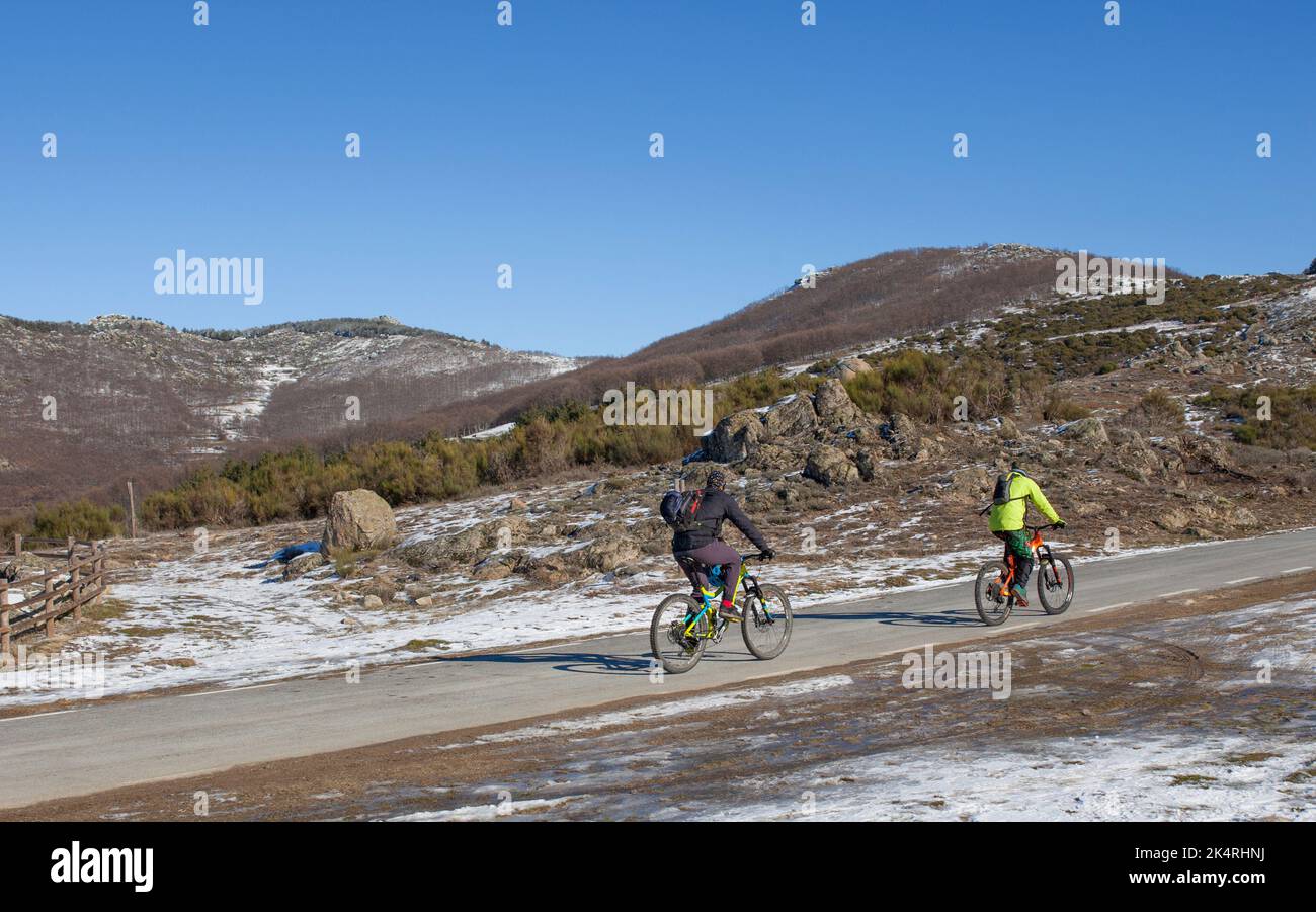 MTB bikers climbing mountain pass. Roadside with snow and ice ponds ...