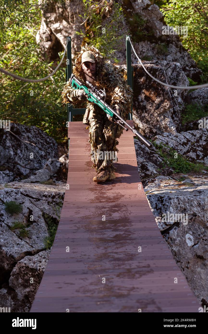 A military man or airsoft player in a camouflage suit sneaking the rope ...
