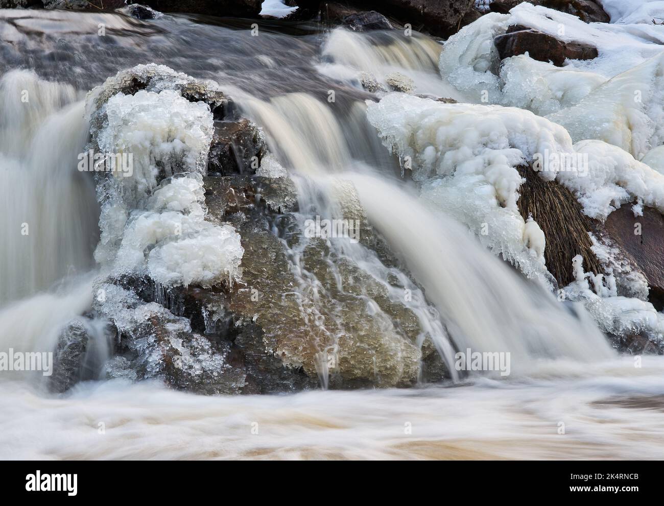A low exposure of water flowing down the rocks covered in snow Stock ...