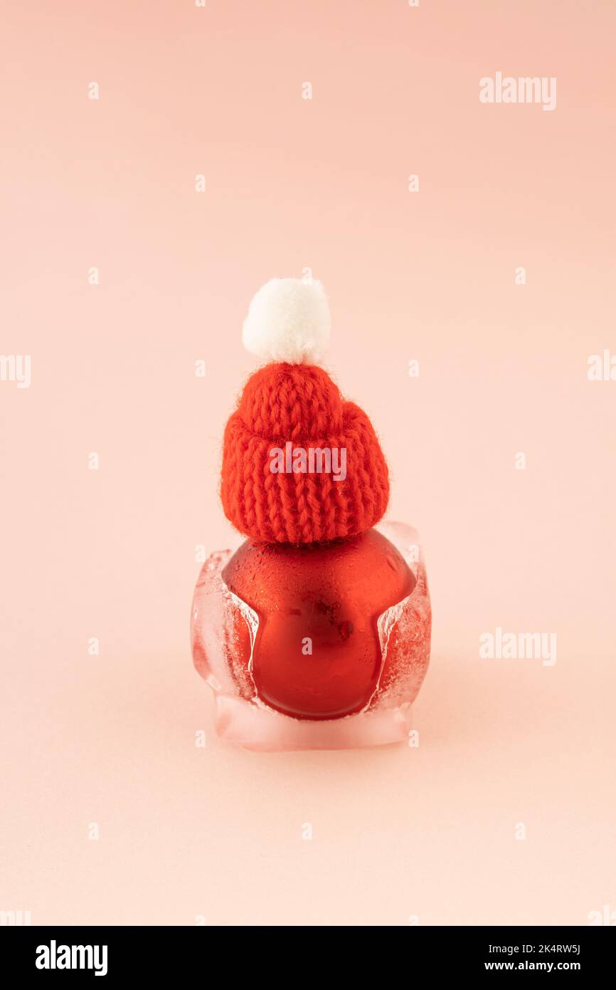 Red Christmas bauble with Santa's hat in melting ice cube on pink ...