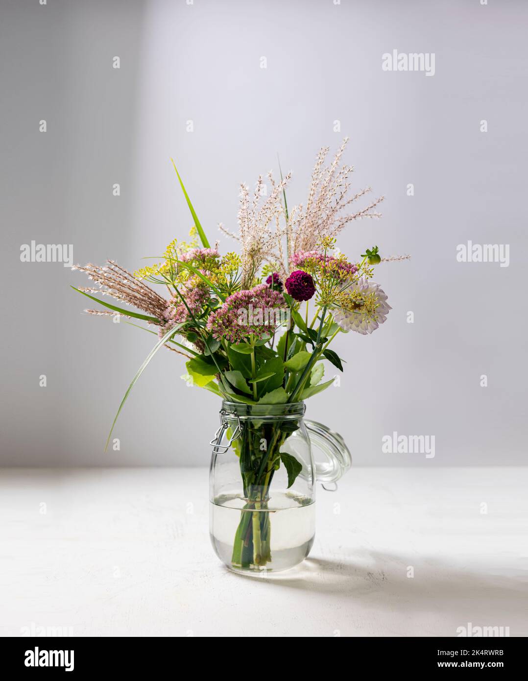 A small minimalist summer bouquet of flowers in glass vase on white ...