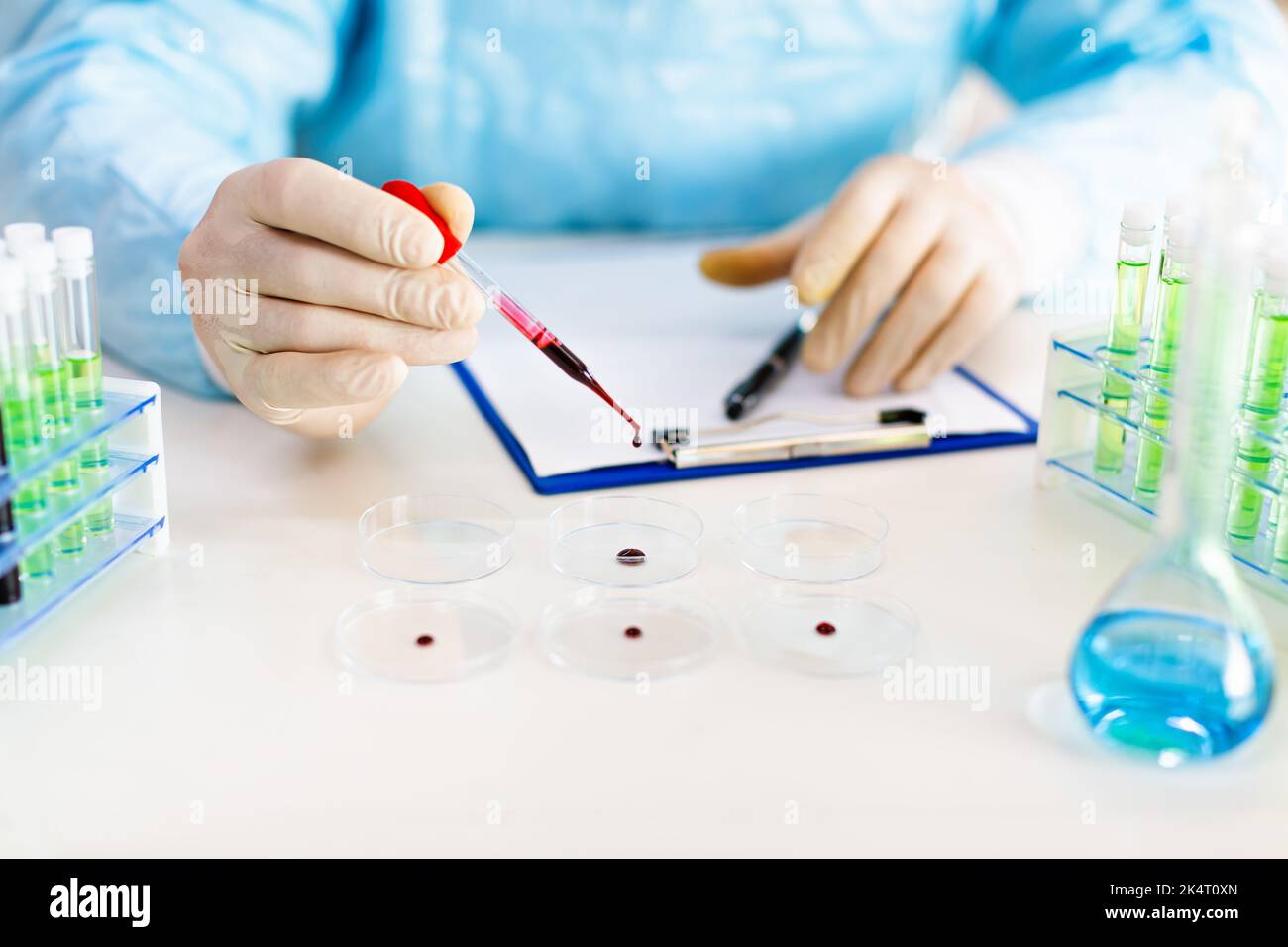 Close-up hands of a researcher in a lab dripping a blood sample in a ...