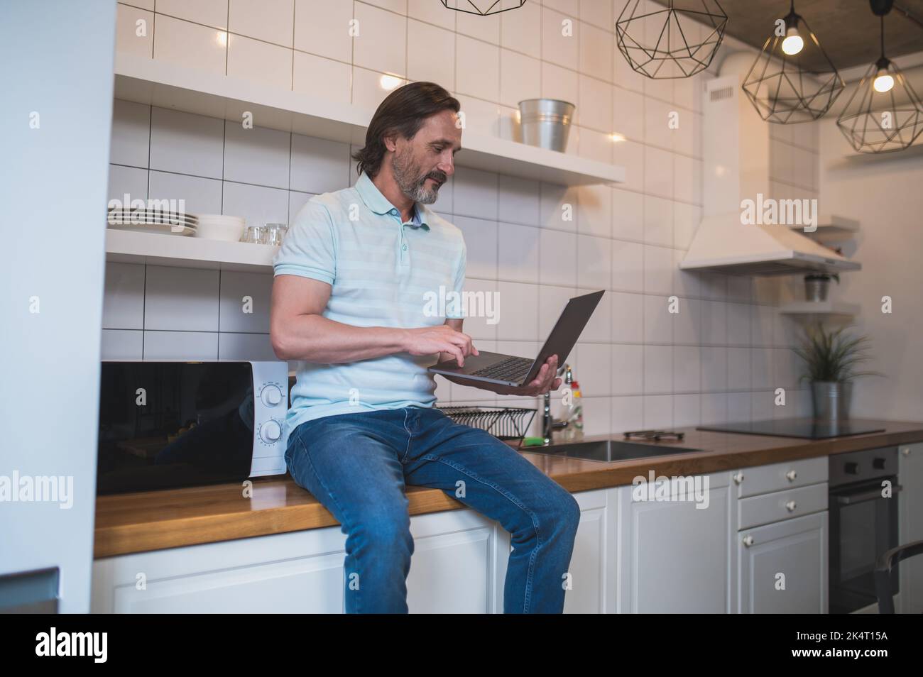 Man sitting on the table in the kitchen with a lapotp Stock Photo - Alamy