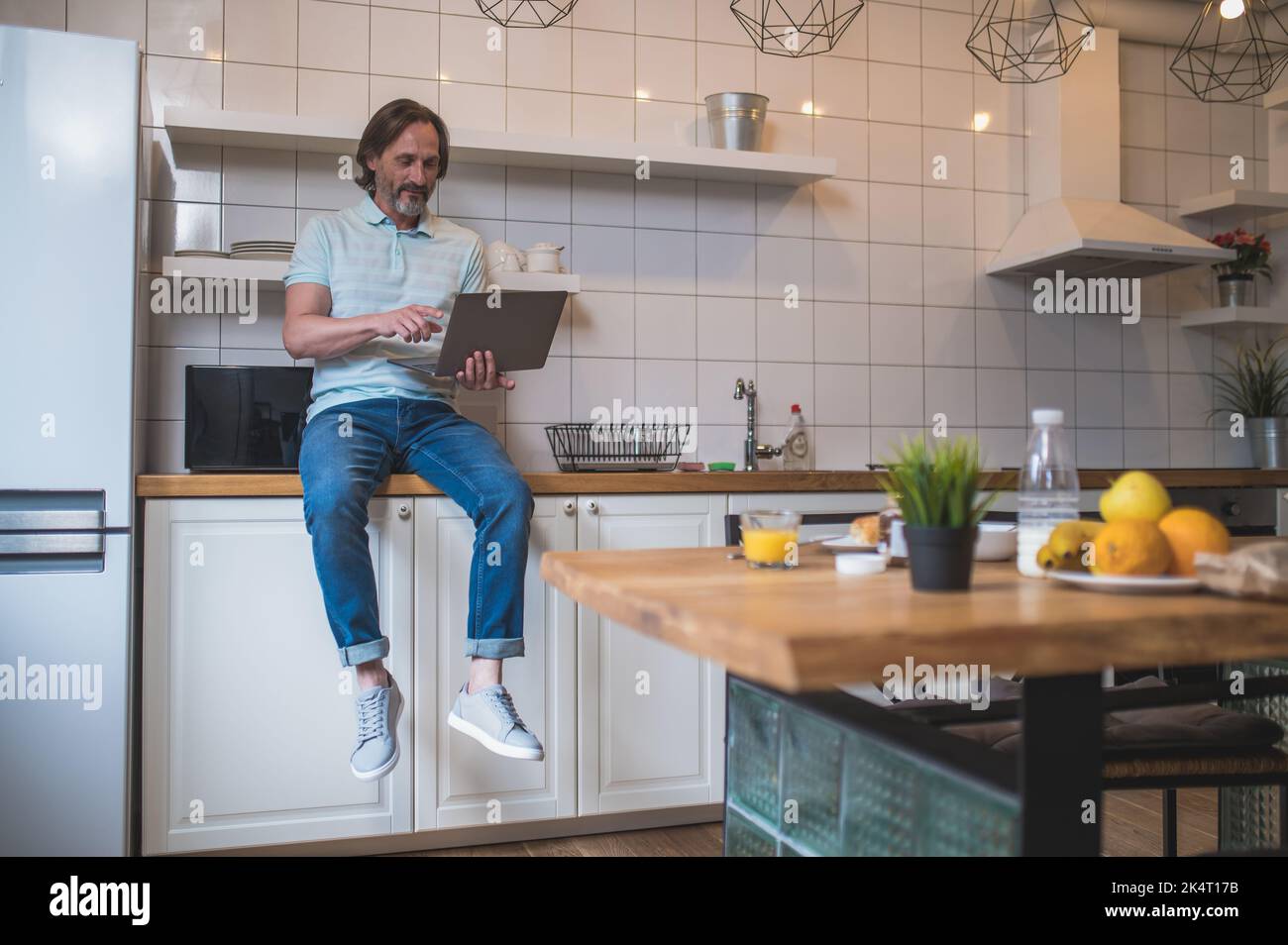 Man sitting on the table in the kitchen with a lapotp Stock Photo - Alamy