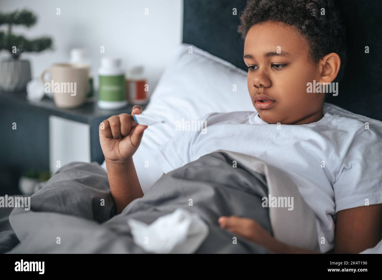 Sick boy lying in bed with fever and checking temperature Stock Photo ...