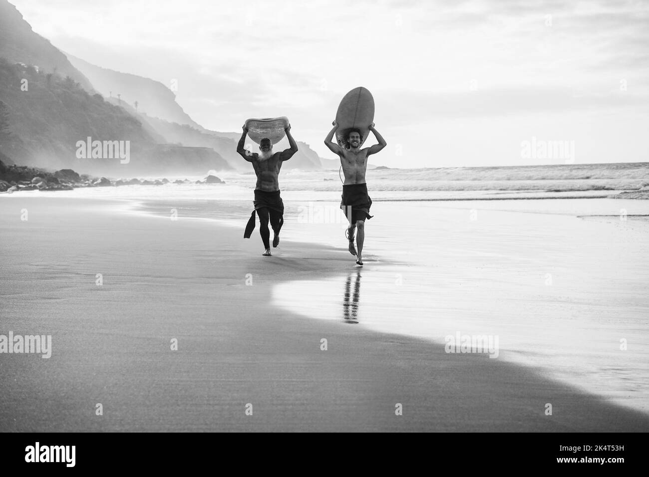 Multi generational surfer friends having fun running on the beach after ...