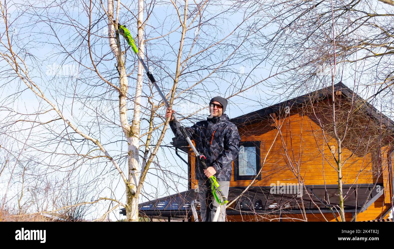 Electric chain pruner with a telescopic pole close up. Winter tree ...