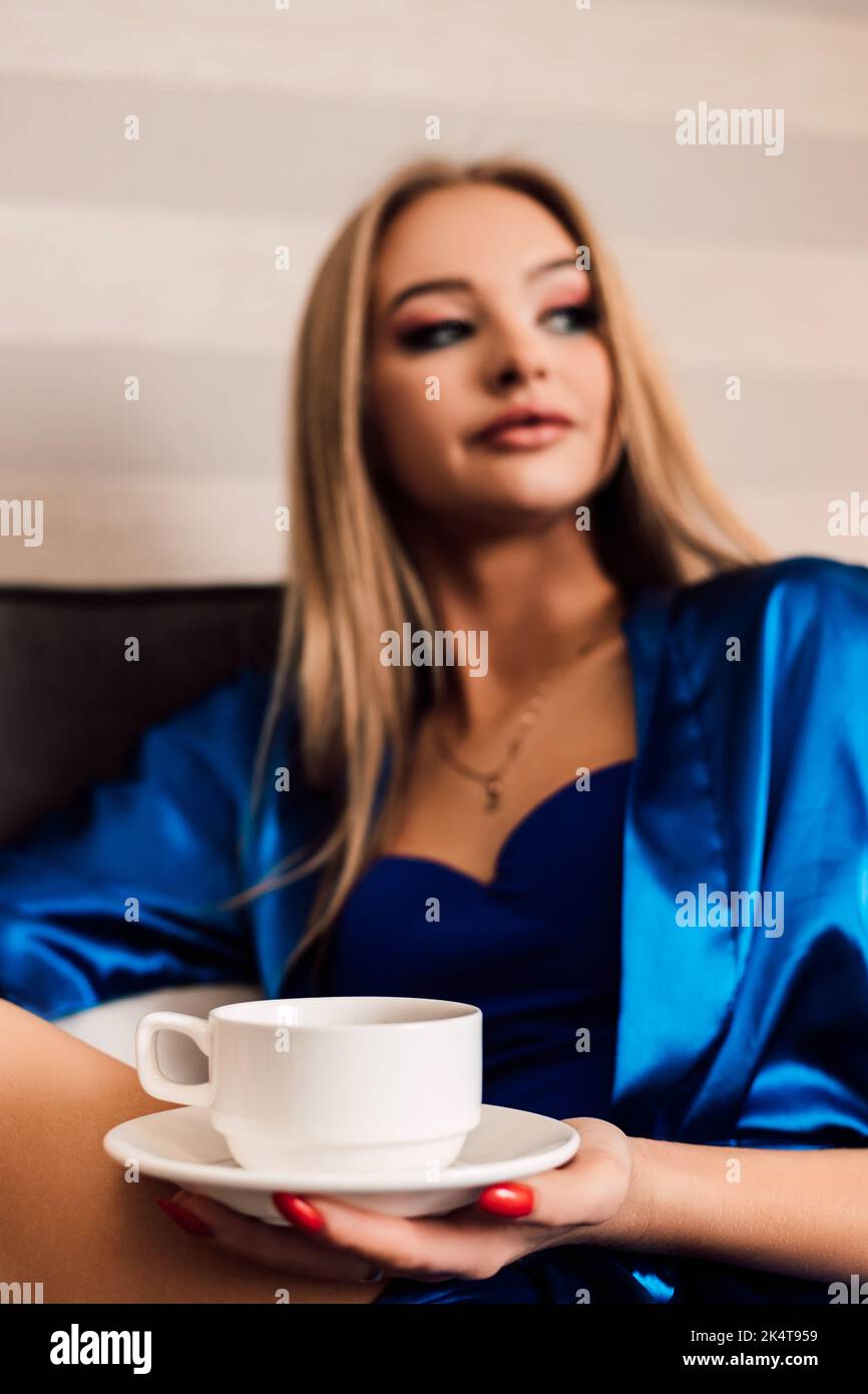 Beautiful girl in a blue bathrobe drinking coffee at home in the ...