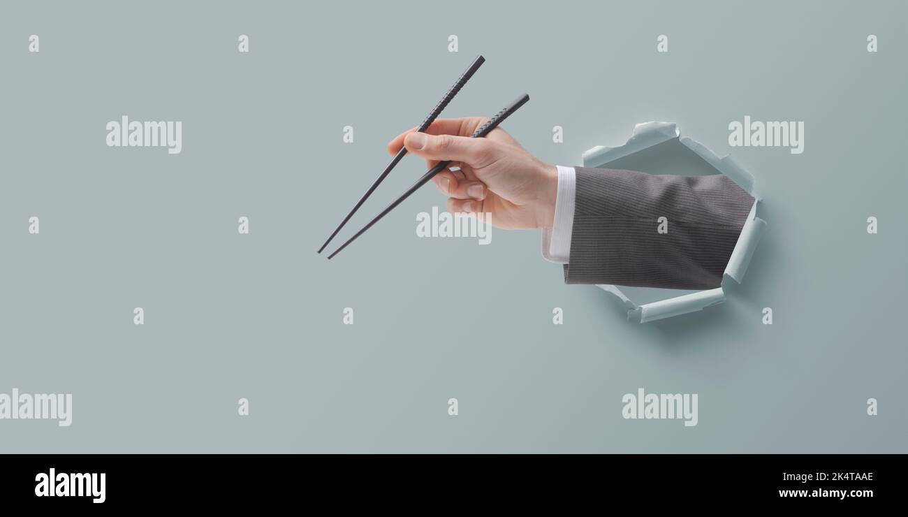 Man holding chopsticks through a hole in paper, asian food and sushi ...