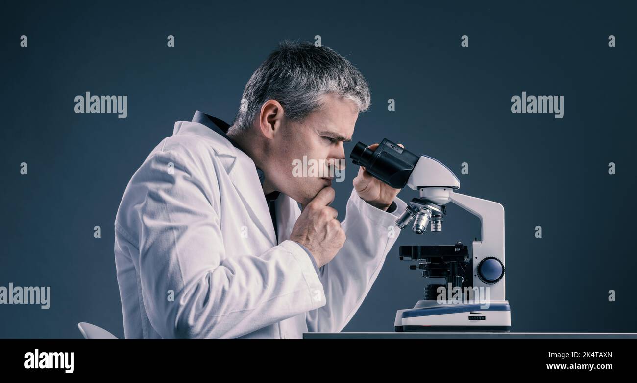 Funny medical scientist working with a microscope, he is focused and ...