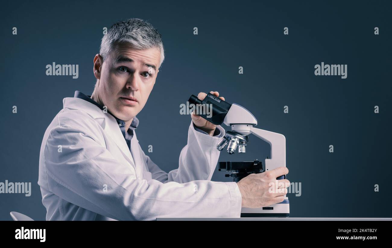 Funny confused medical scientist working with a microscope, he made an ...