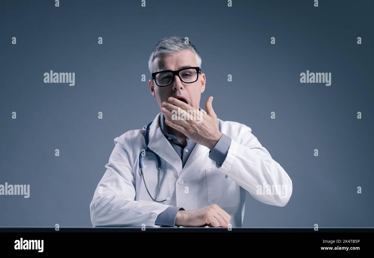 Sleepy overworked doctor yawning and covering his mouth with his hand ...