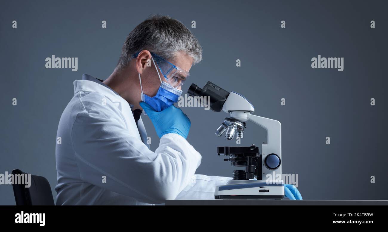 Scientist with face mask examining a sample under the microscope and ...