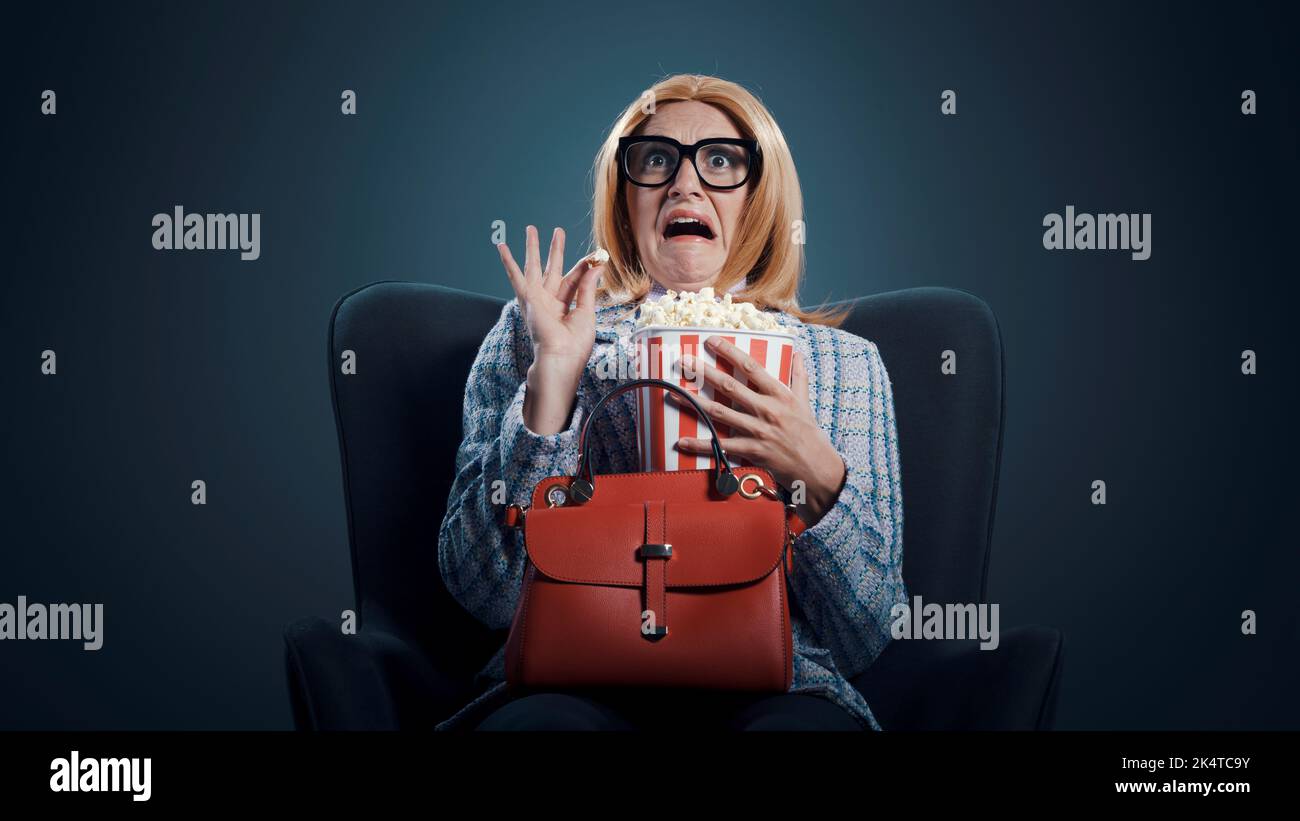 Funny scared woman watching a horror movie and eating popcorn, cinema ...