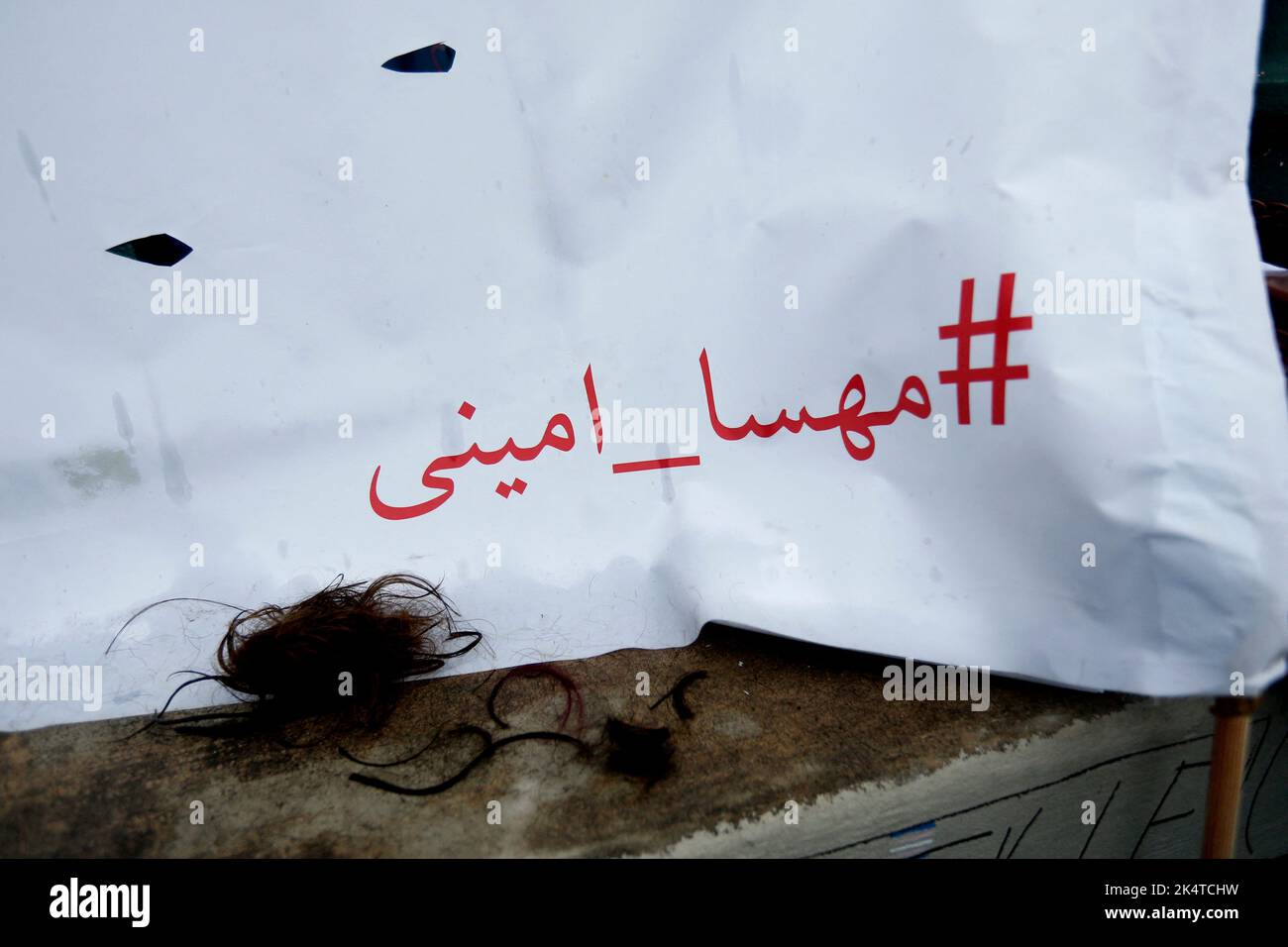 A bunch of hair cut by a protestor lays next to the hashtag Mahsa Amini ...