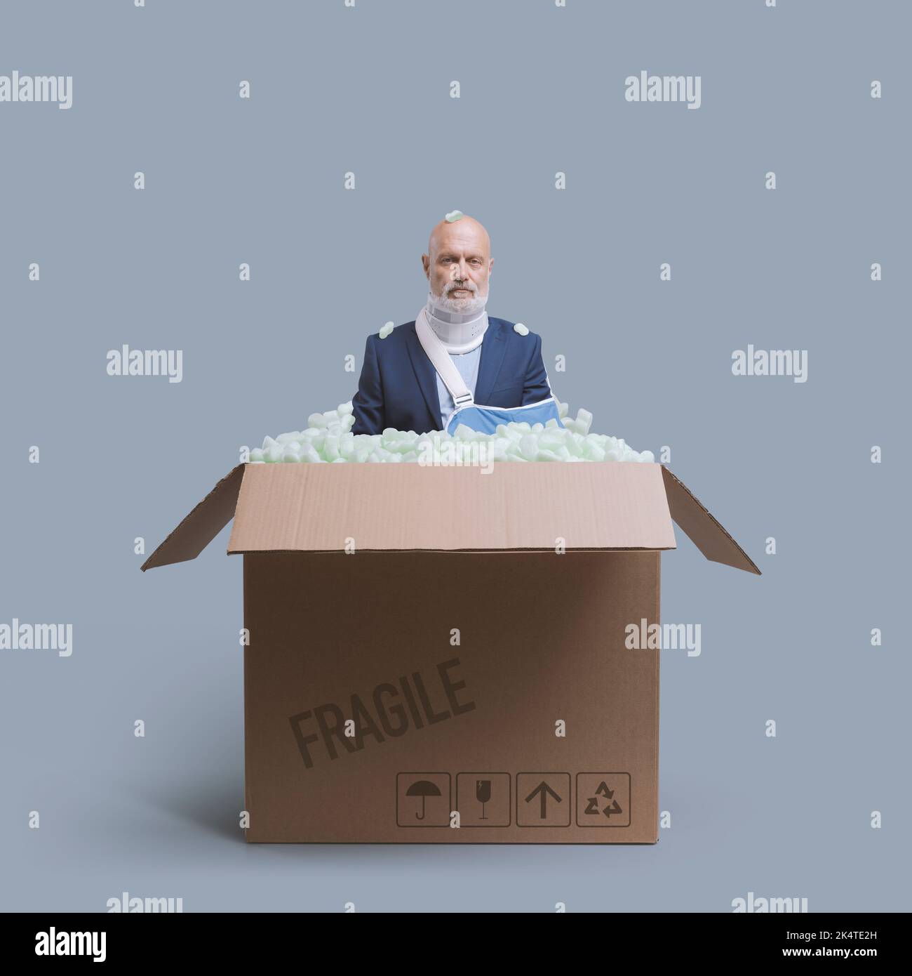 Sad injured man with cervical collar and broken arm in a delivery box ...