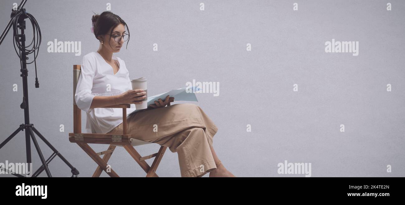 Focused actress sitting on the director's chair and reading a play ...