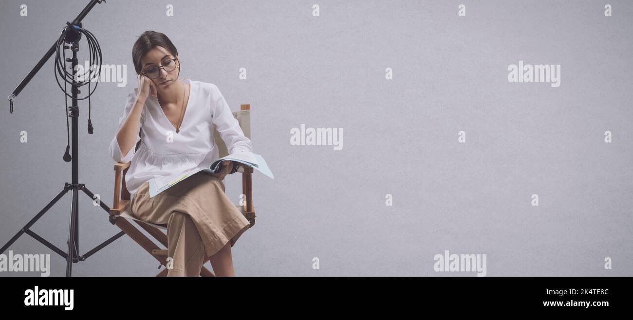 Focused film director sitting on the director's chair and reading a ...