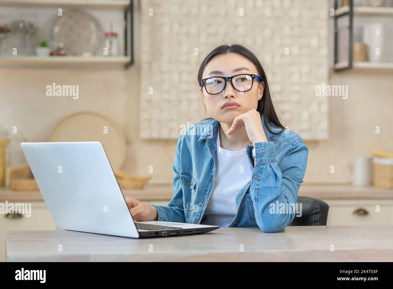 Sad and upset woman sitting at home in the kitchen, asian woman with ...
