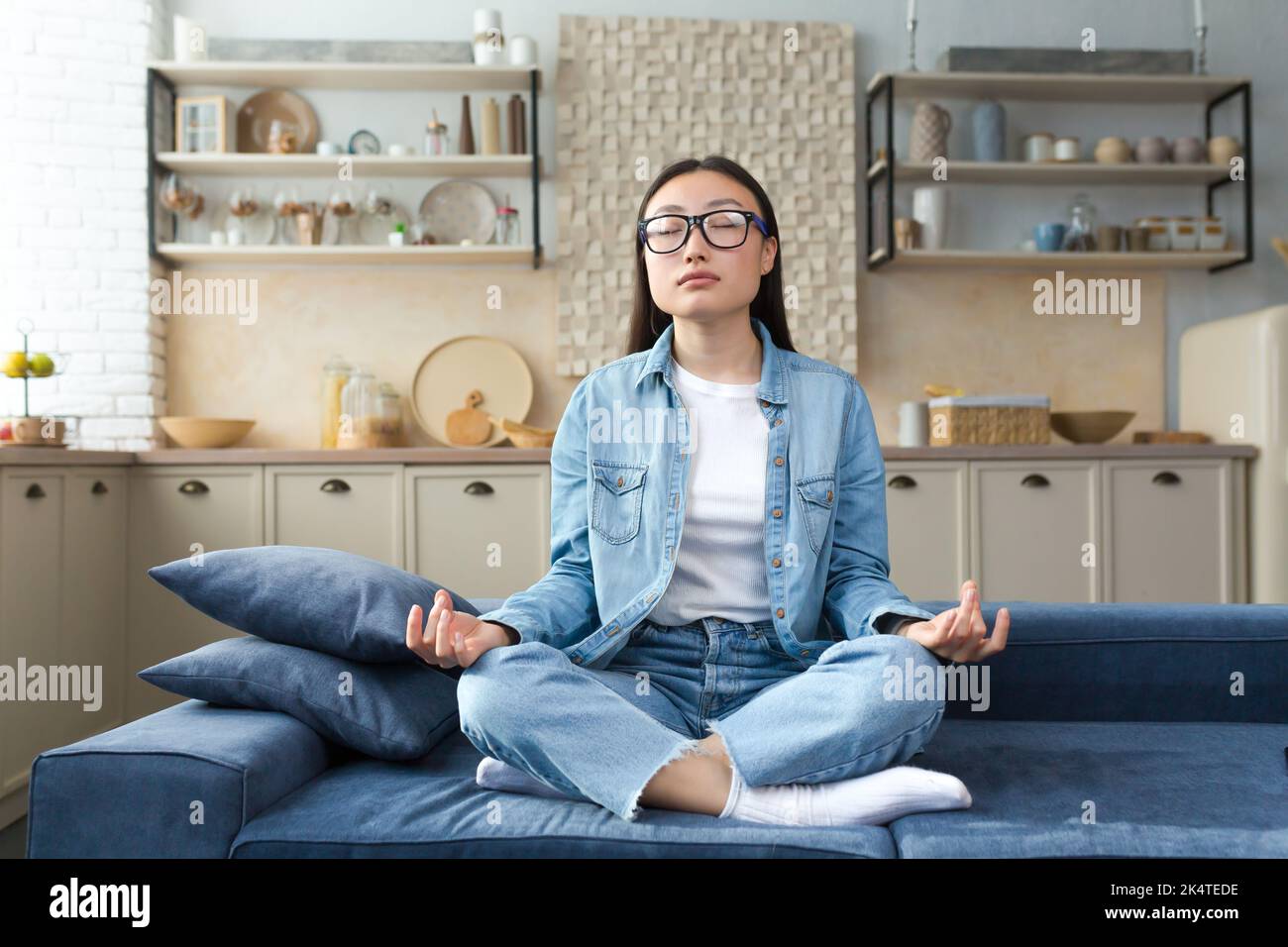 Beautiful Asian woman relaxing at home sitting on sofa and meditating ...