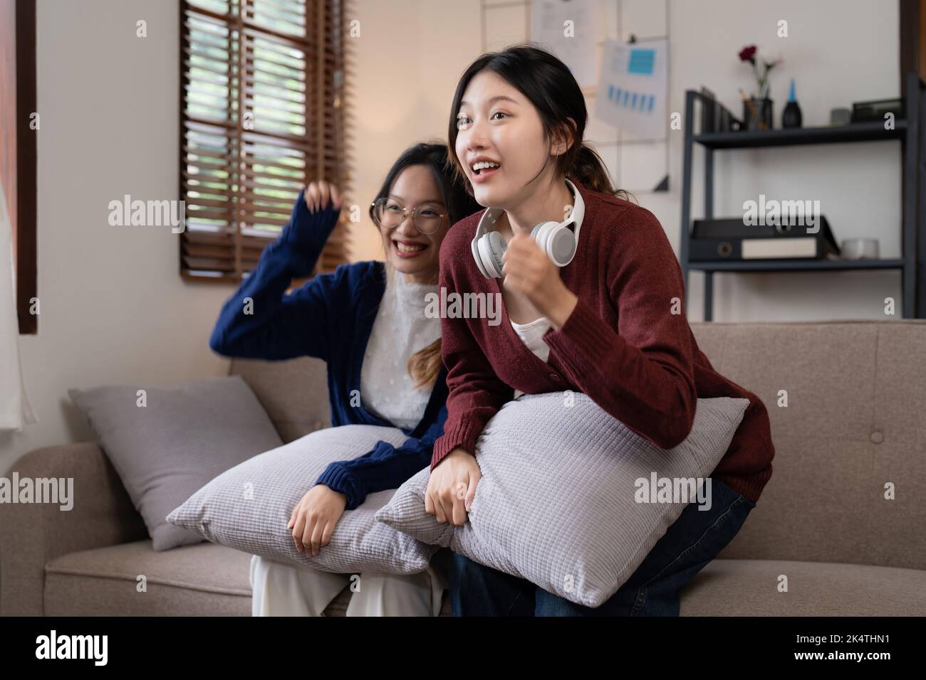 Two Young woman cheering together for sport on TV in cozy living room ...