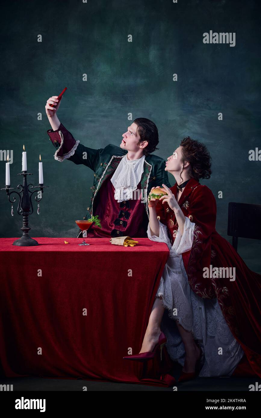 Portrait of man and woman in image of vampires taking selfie over dark ...
