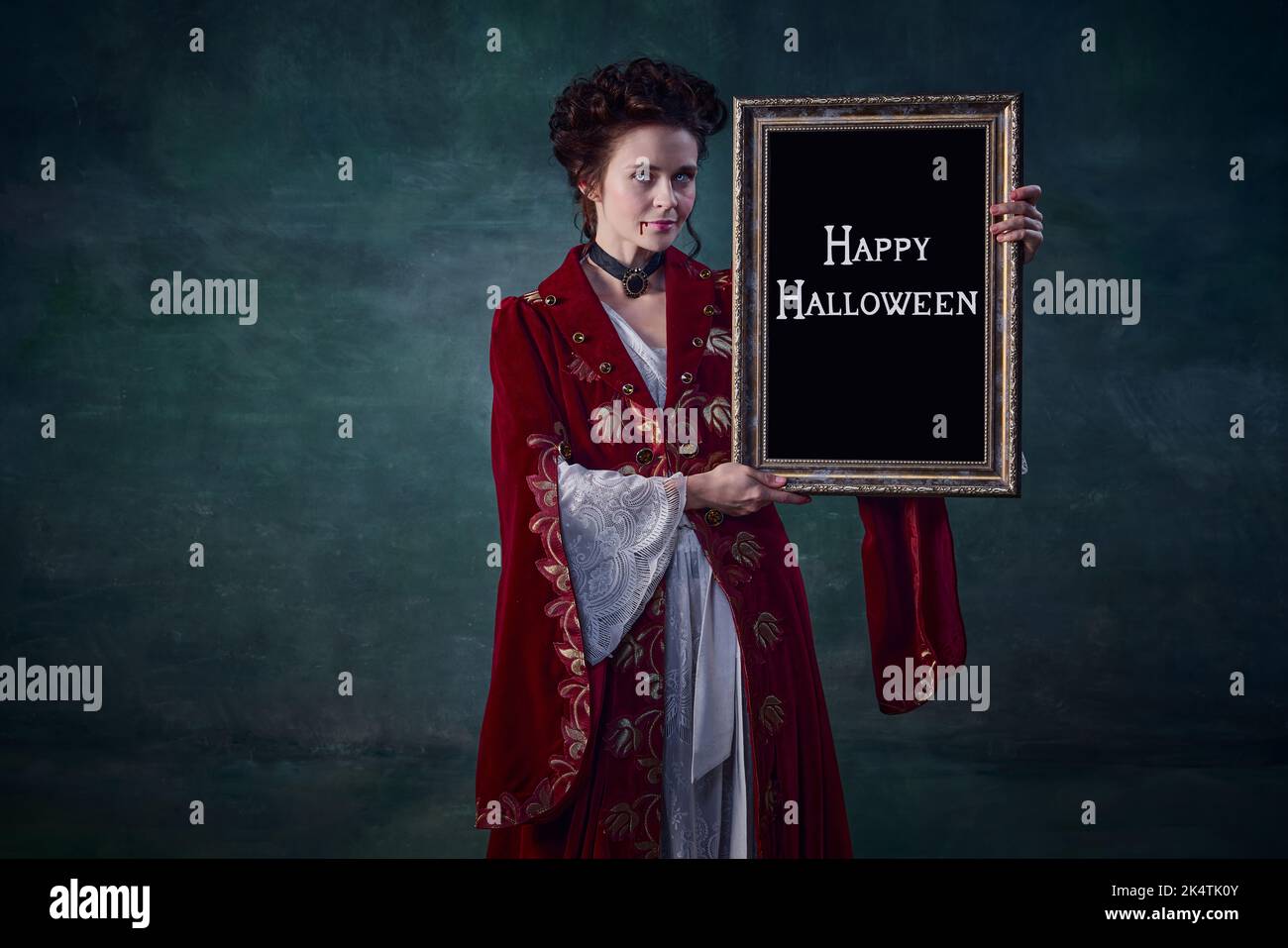 Portrait of young attractive woman in image of vampire holding picture ...