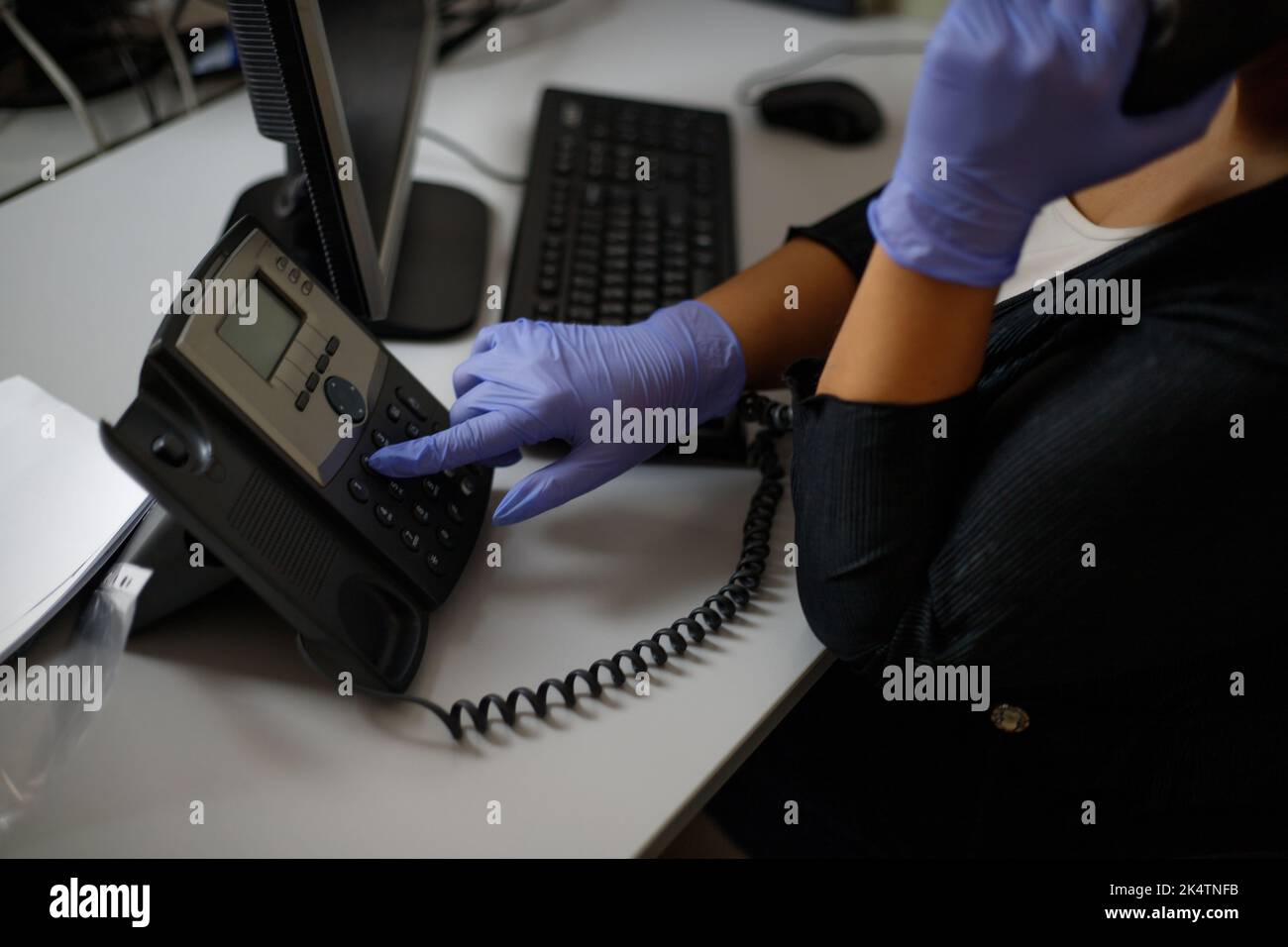 An employee in the office makes a call on a landline phone wearing ...