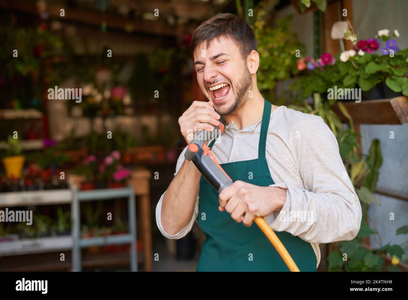 Cheerful gardener apprentice with garden hose sings out of high spirits ...