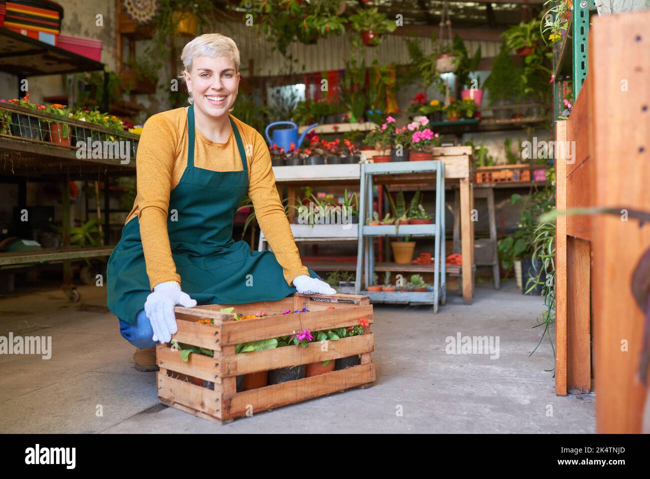 Happy young woman gardener holding box of flowers for shipping or ...