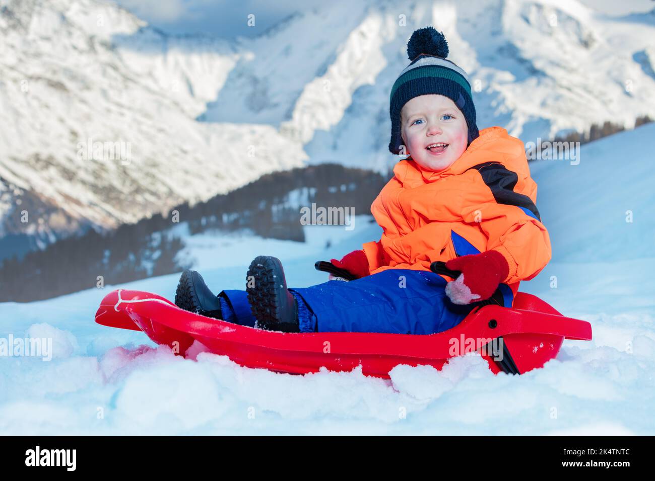 Little boy sit on sledge in show over mountains going downhill Stock ...