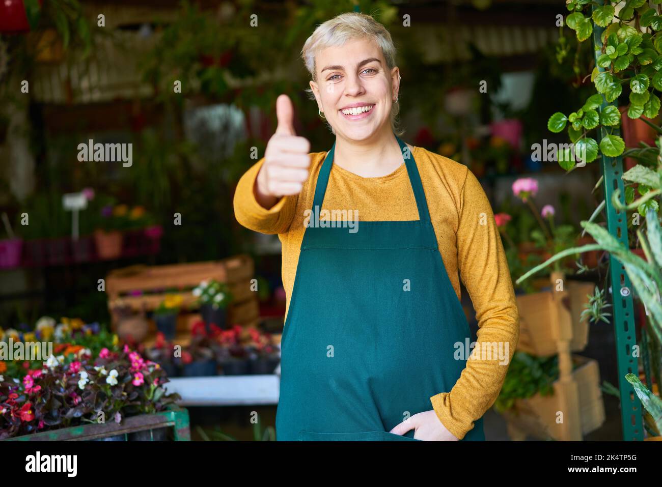 Young woman gardener and start-up founder with thumbs up in her flower ...