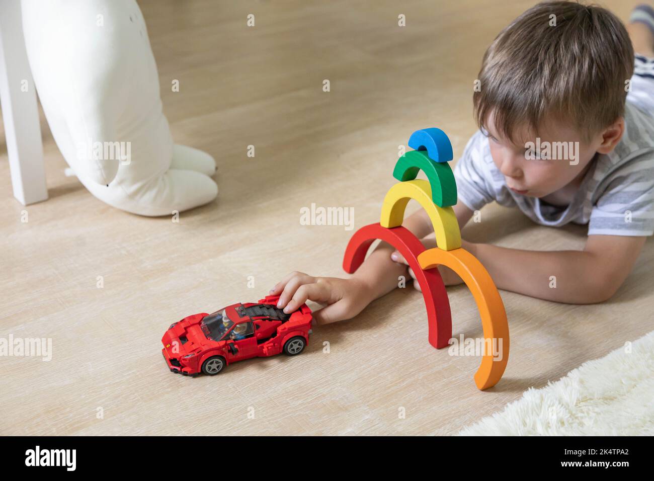 Smiling male kid playing red car automobile toy with Montessori rainbow ...