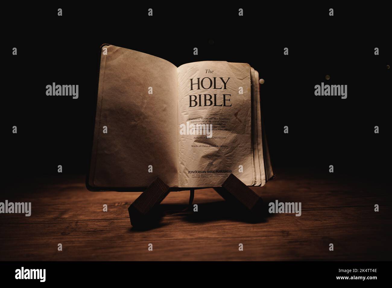 An old Holy Bible book on a wooden stand illuminated by a light falling ...