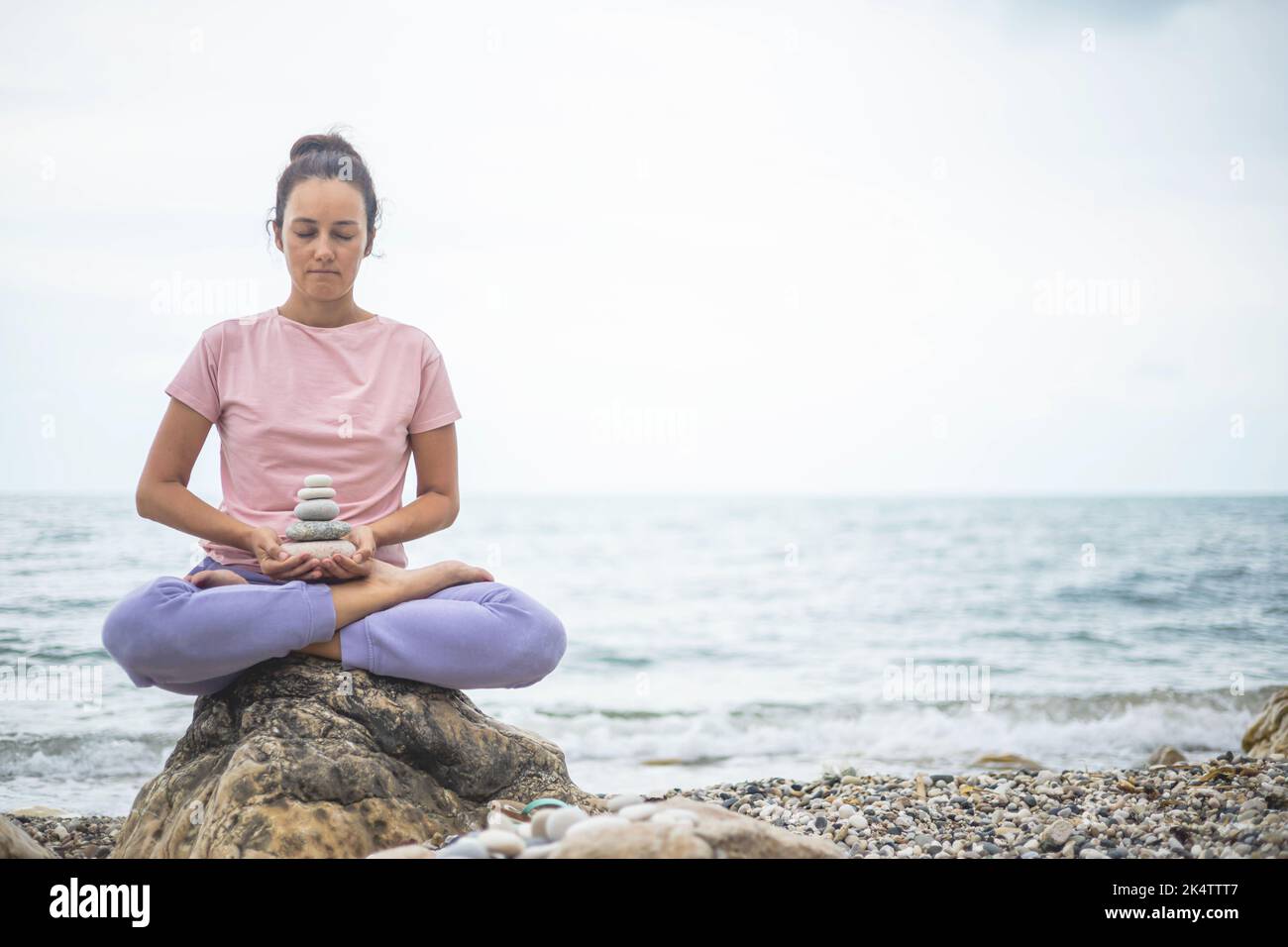 Spiritual yoga woman lotus position on cobblestone with pebble tower ...