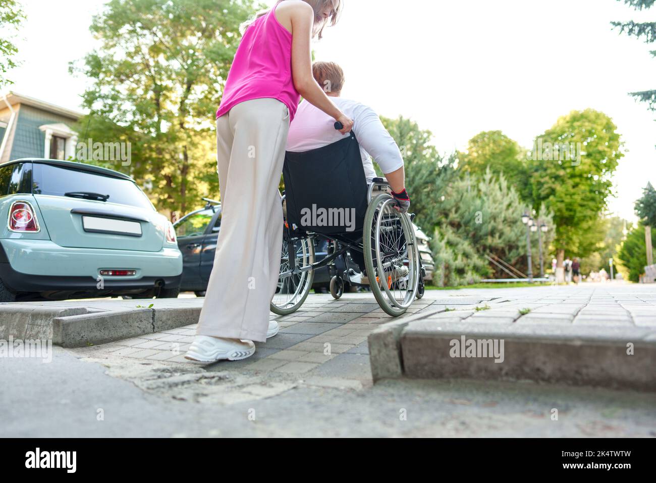 Young female caregiver pushing wheelchair with female person with ...