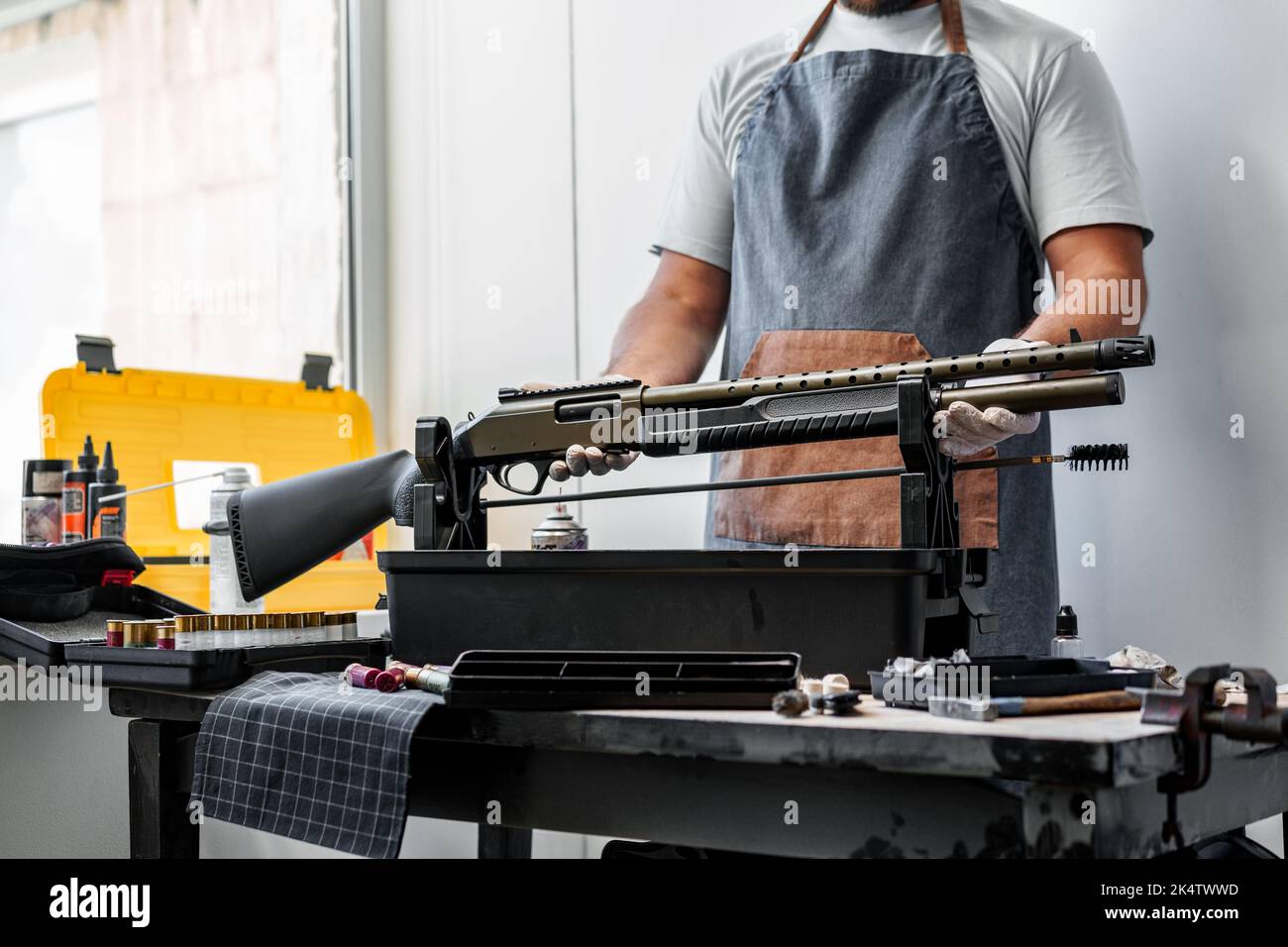 Close up of young man in apron disassembling a gun above the table ...