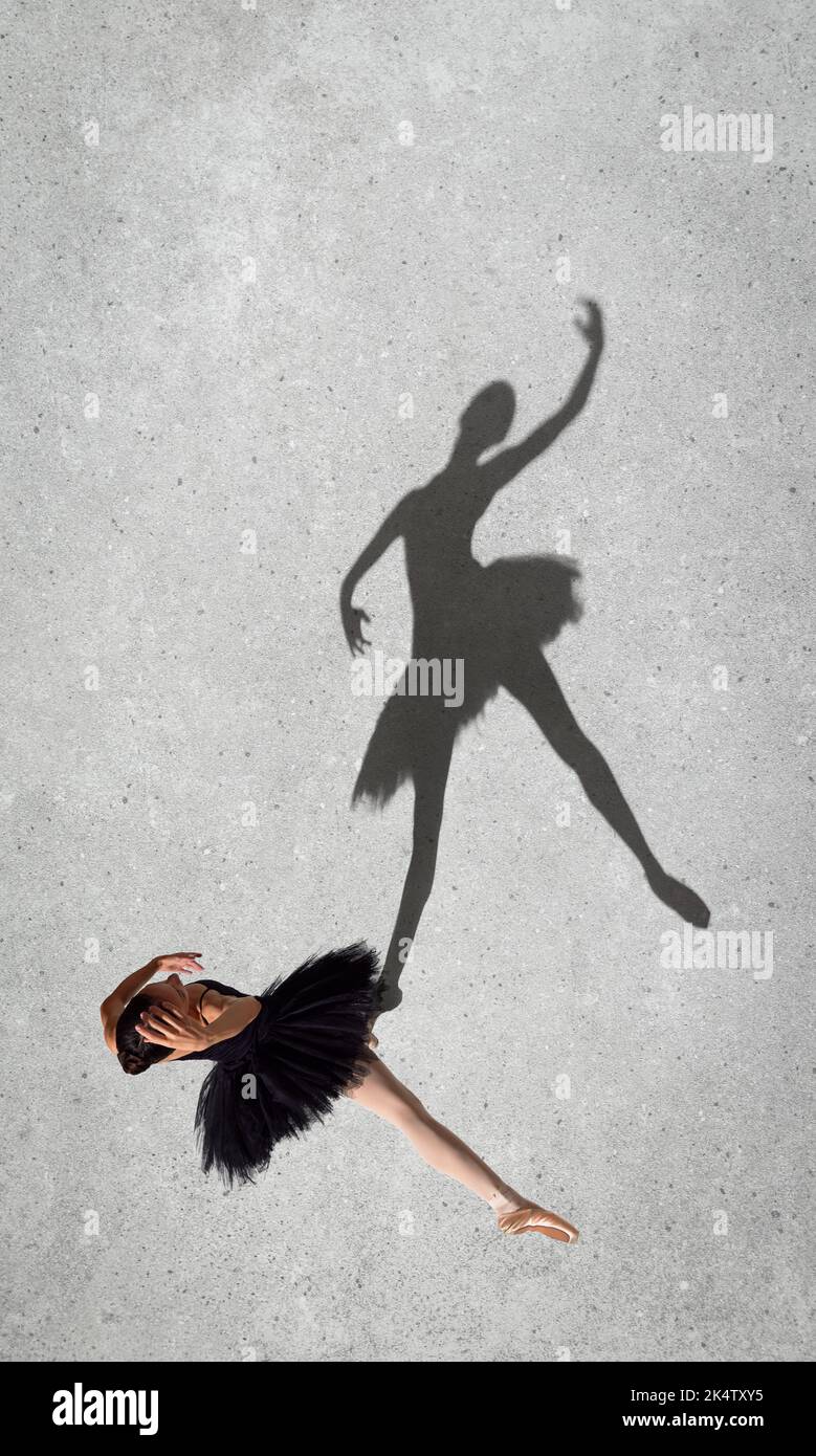 Portrait of young ballerina in black dress dancing isolated over grey wall background. Top view ...