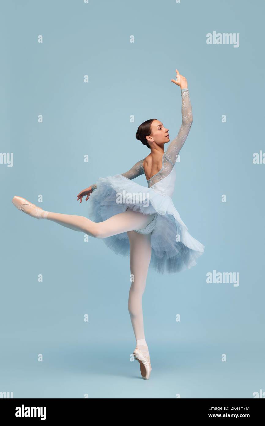 Portrait of tender young ballerina dancing, performing isolated over blue studio background ...