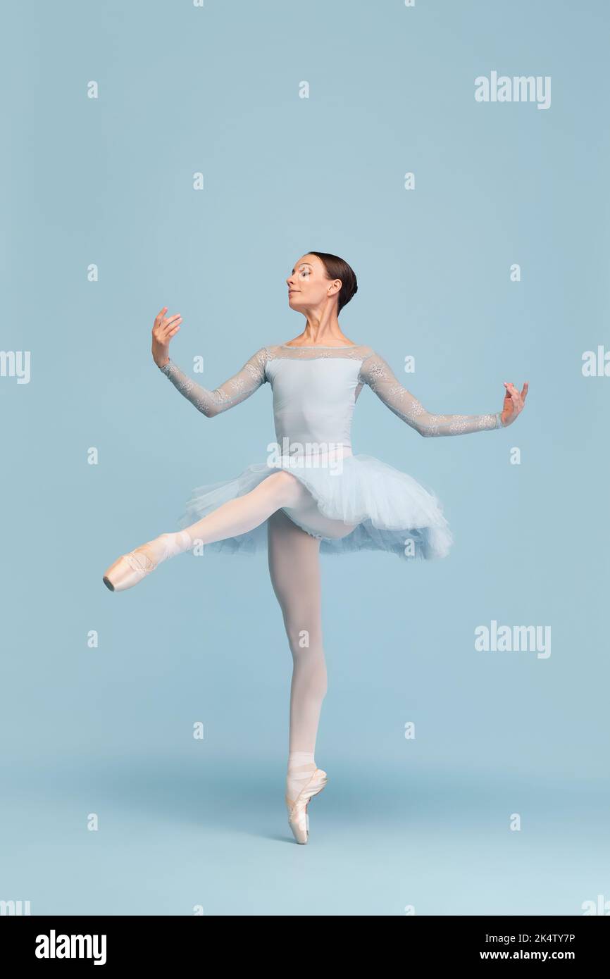 Portrait of tender young ballerina dancing, performing isolated over blue studio background ...