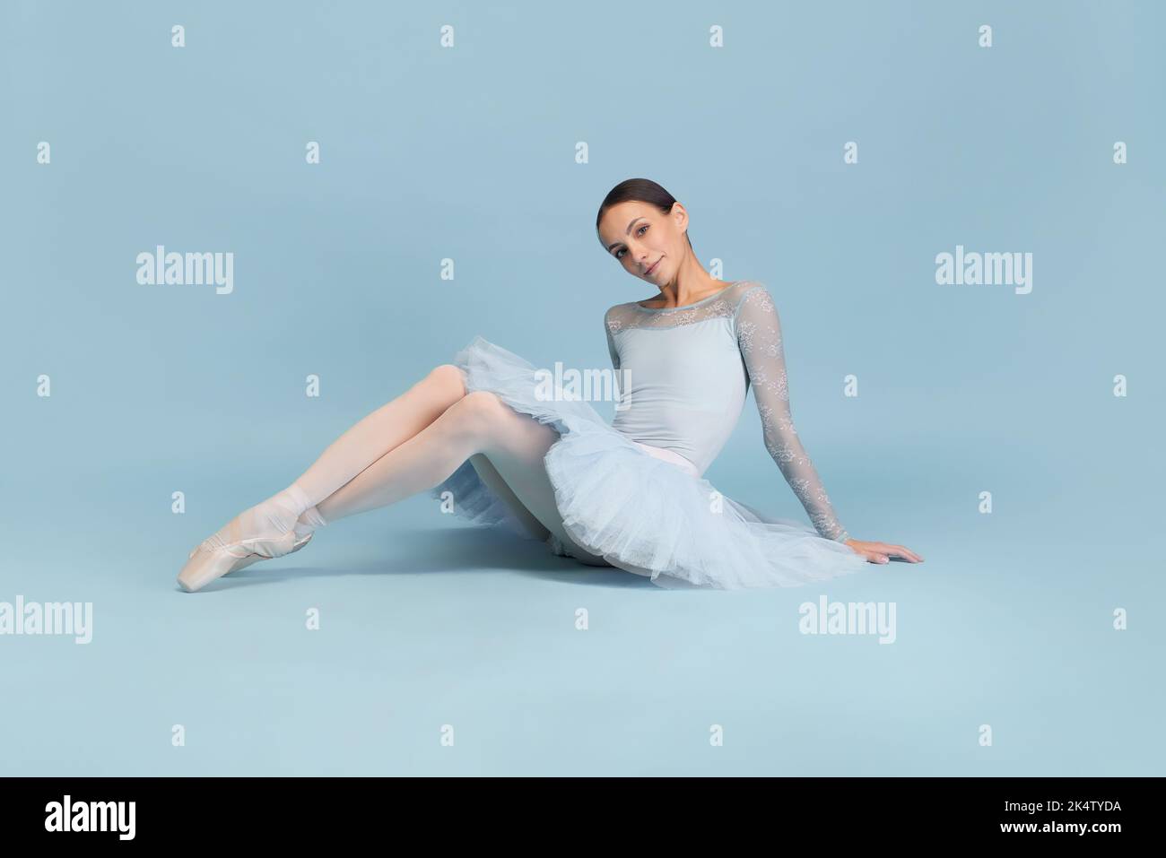 Portrait of tender young ballerina dancing, performing isolated over blue studio background ...