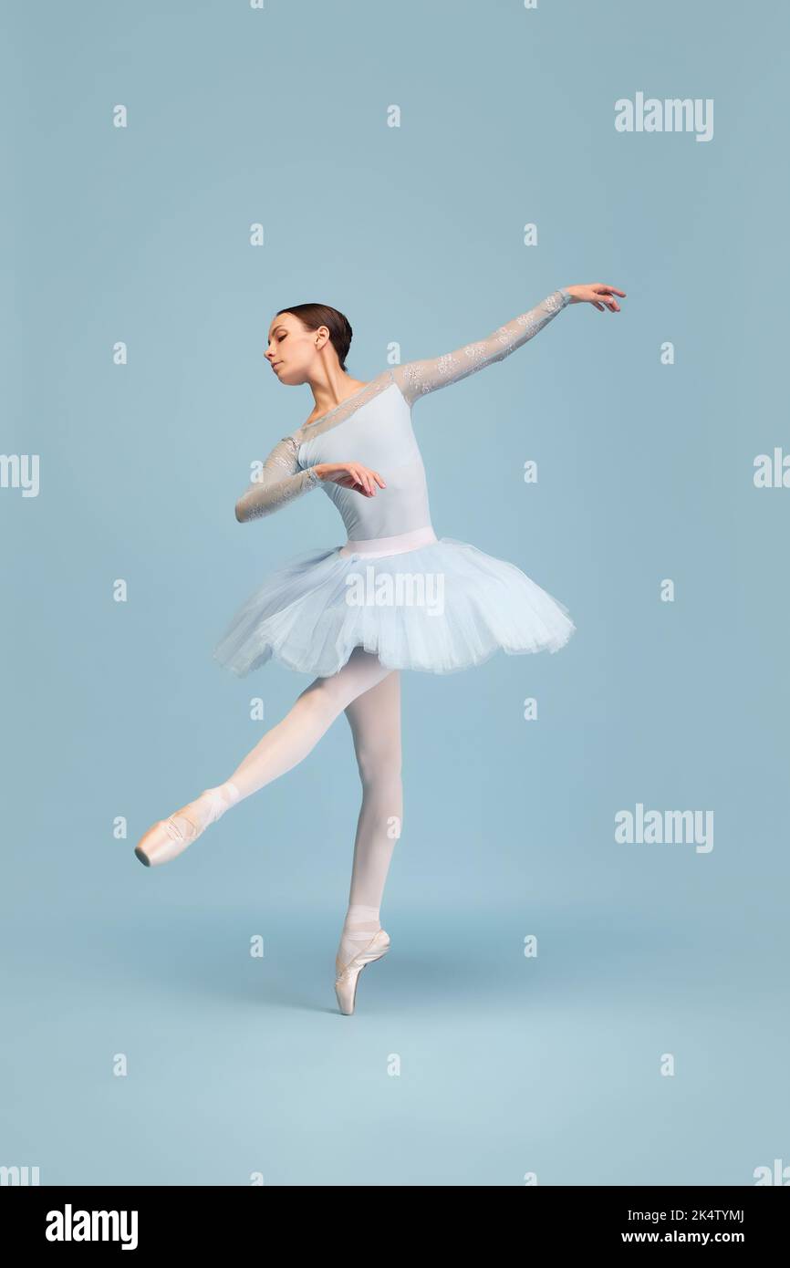 Portrait of tender young ballerina dancing, performing isolated over blue studio background ...