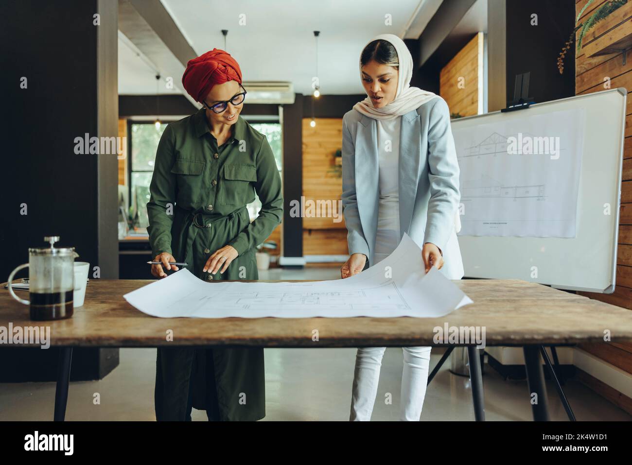 Innovative Muslim architects working on blueprint drawings in a modern office. Two businesswomen ...