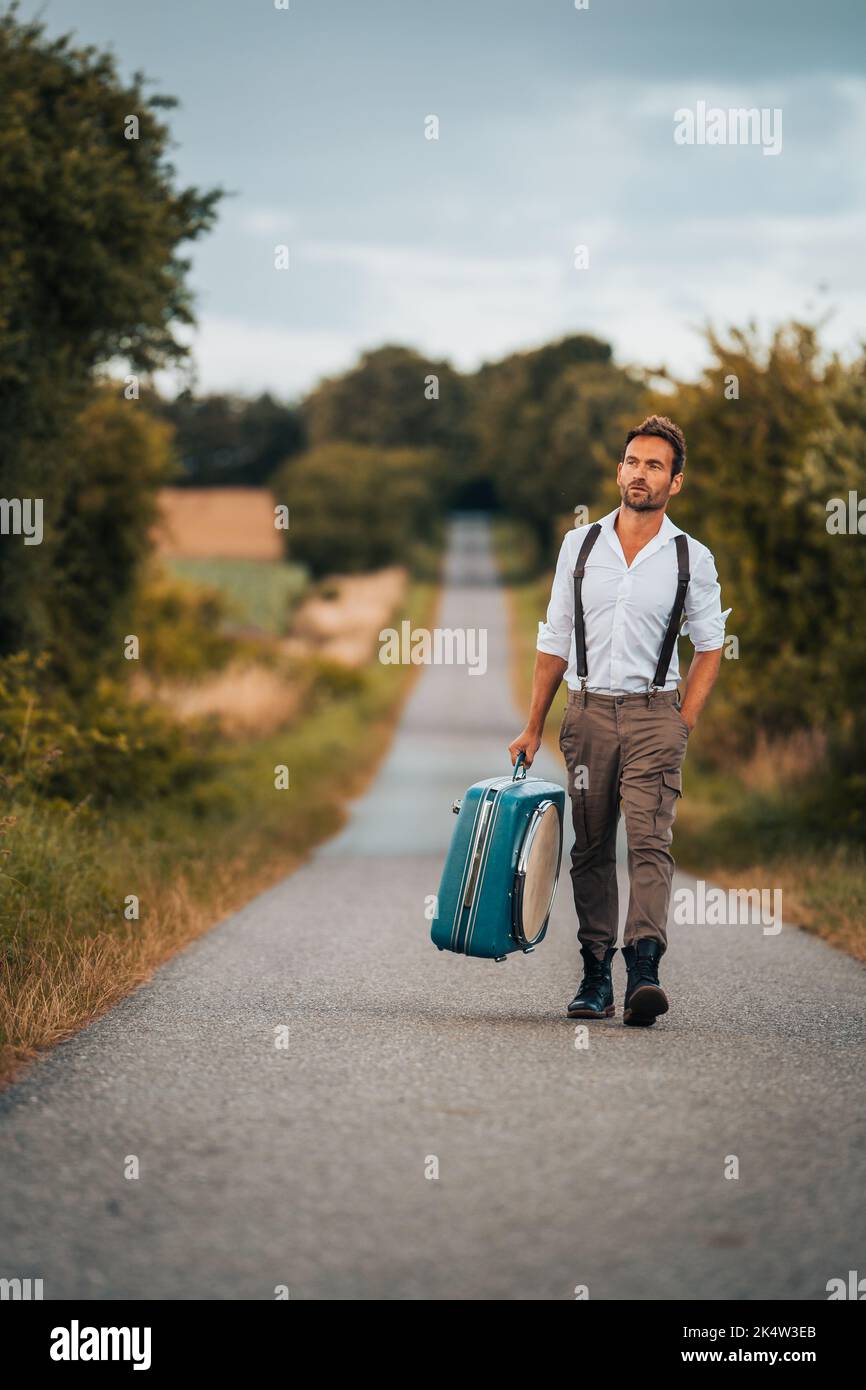 Individual man in vintage clothing holding a suitecase is walking along ...
