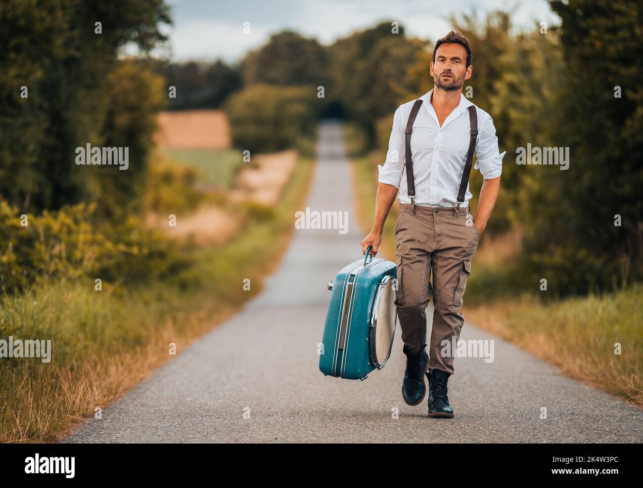 Individual man in vintage clothing holding a suitecase is walking along ...