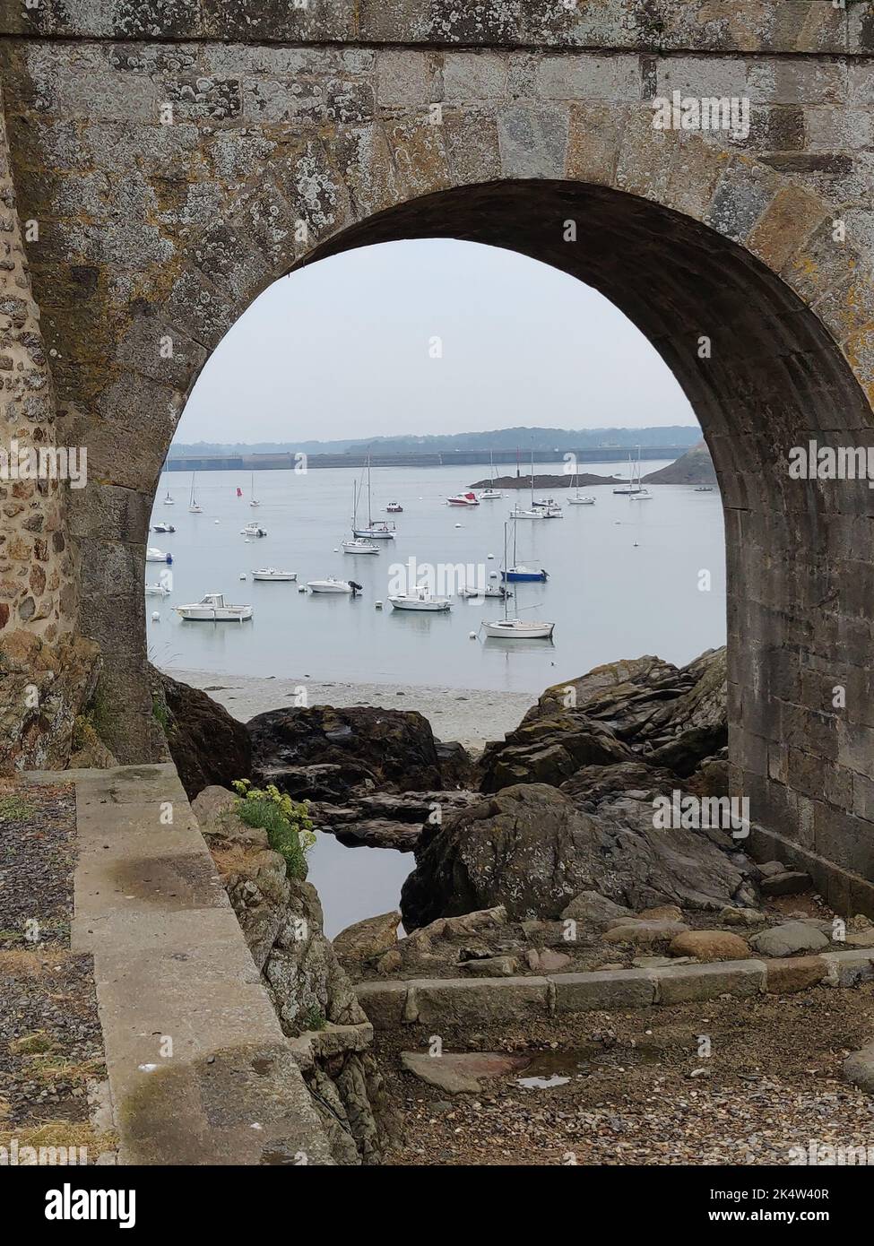 A vertical shot of a stone arch with boats in the background Stock ...