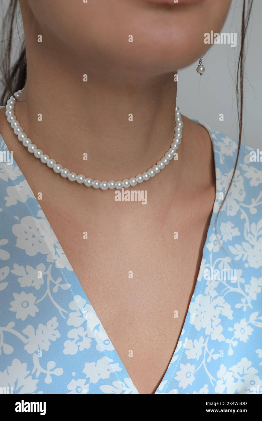 A vertical closeup of a pearl necklace around a Caucasian female's neck ...