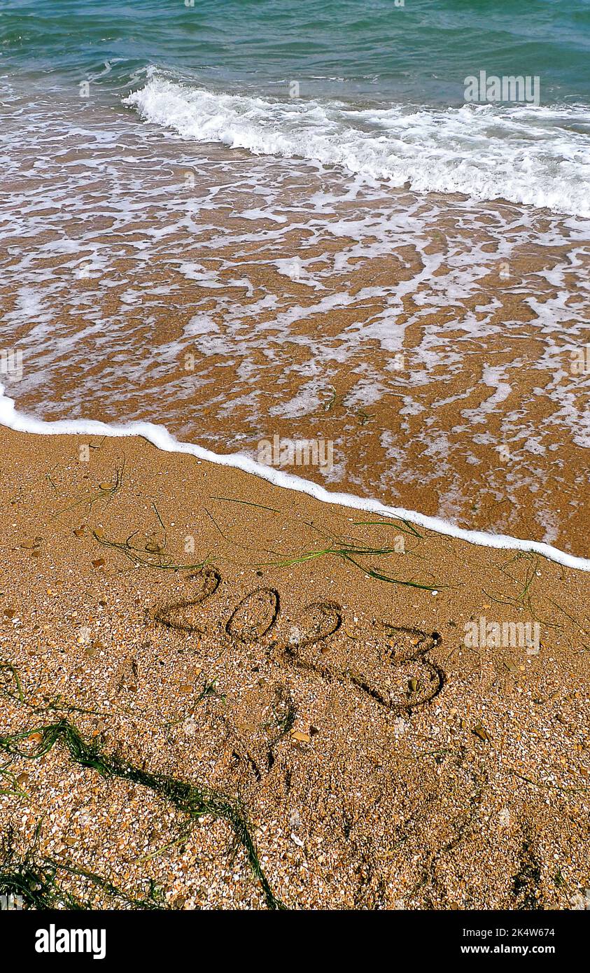 2023 written on the beach sand. Bright turquoise green sea waves with ...