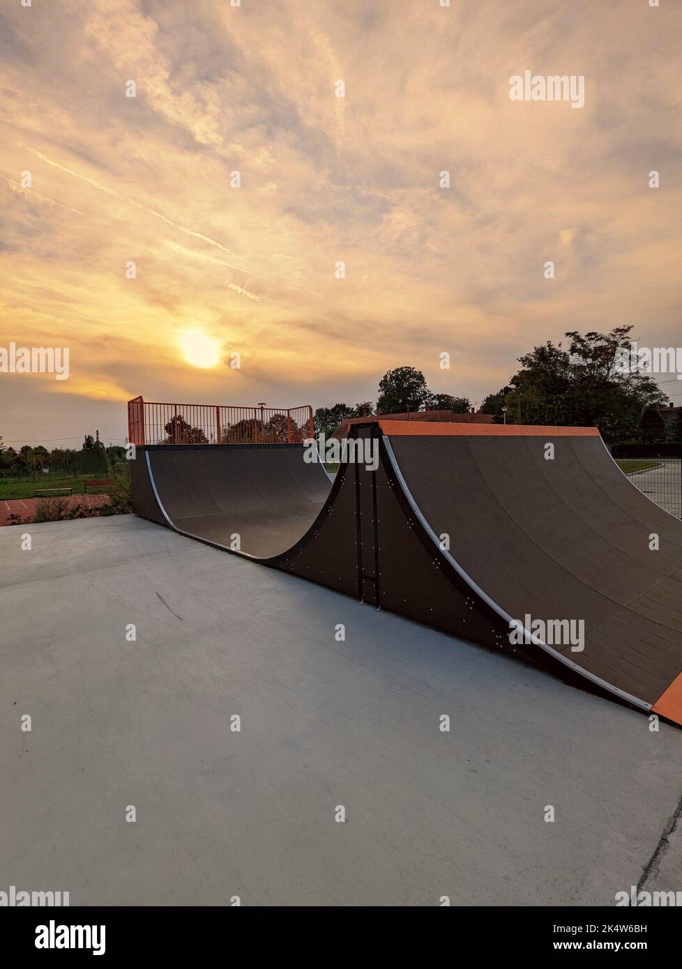 A vertical shot of half pipe in a skate park on bright sunset sky ...