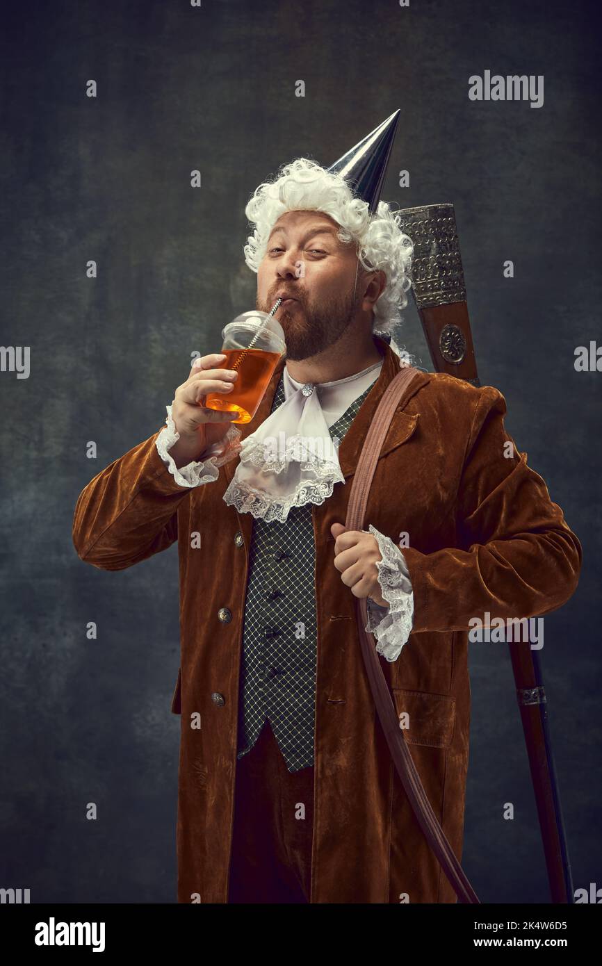 Sweet drinks. Smiling young man in brown vintage suit and white wig ...